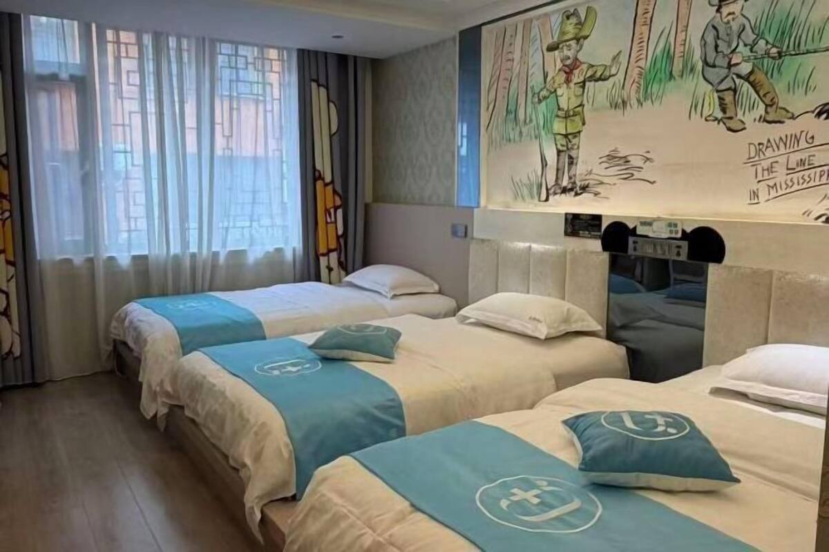Quarto de hotel com duas camas, um mural na parede e uma janela com cortinas.