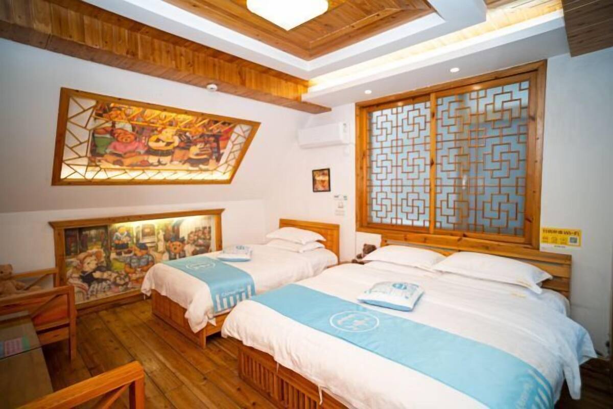 Quarto com duas camas, piso de madeira, uma janela grande com padrão geométrico e teto com vigas de madeira e iluminação embutida.