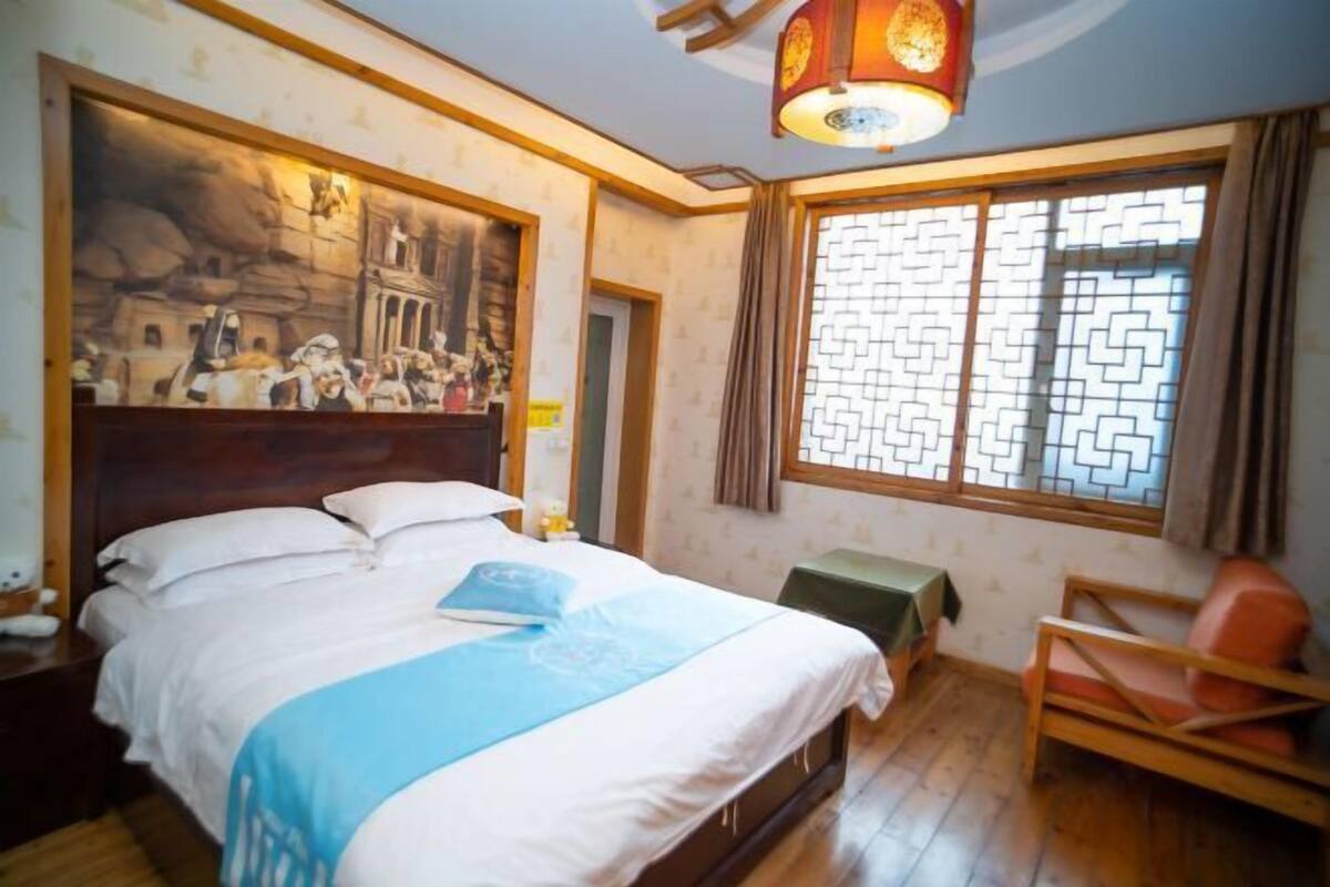 Quarto com cama, mesa de cabeceira, cadeira, janela com padrão geométrico e um quadro na parede.