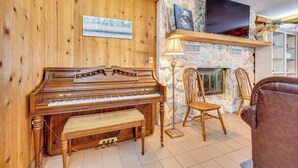 Um piano de madeira, uma lareira de pedra, uma televisão e uma poltrona de couro marrom numa sala de estar.
