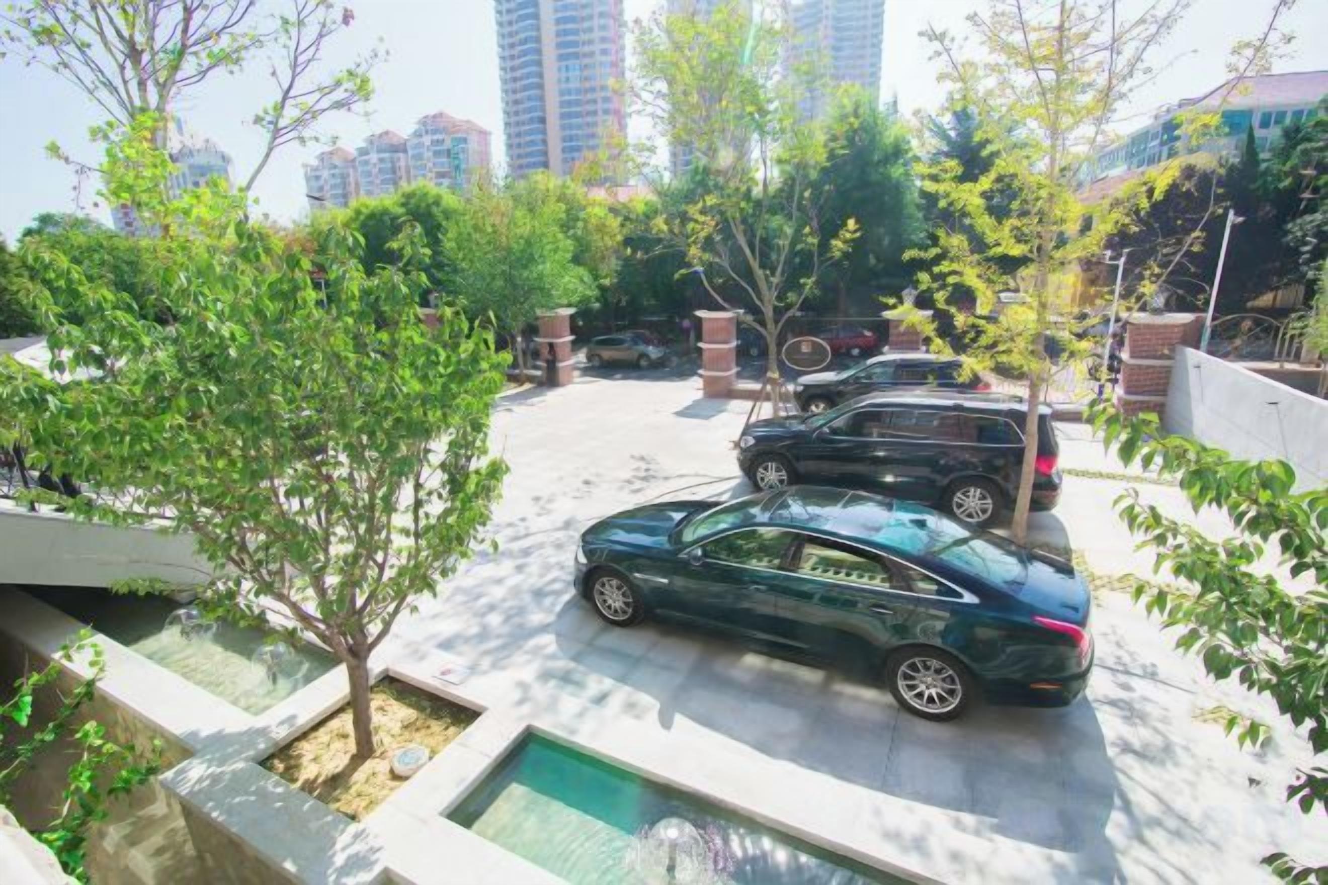 Uma área de estacionamento com dois carros, árvores e um edifício ao fundo.