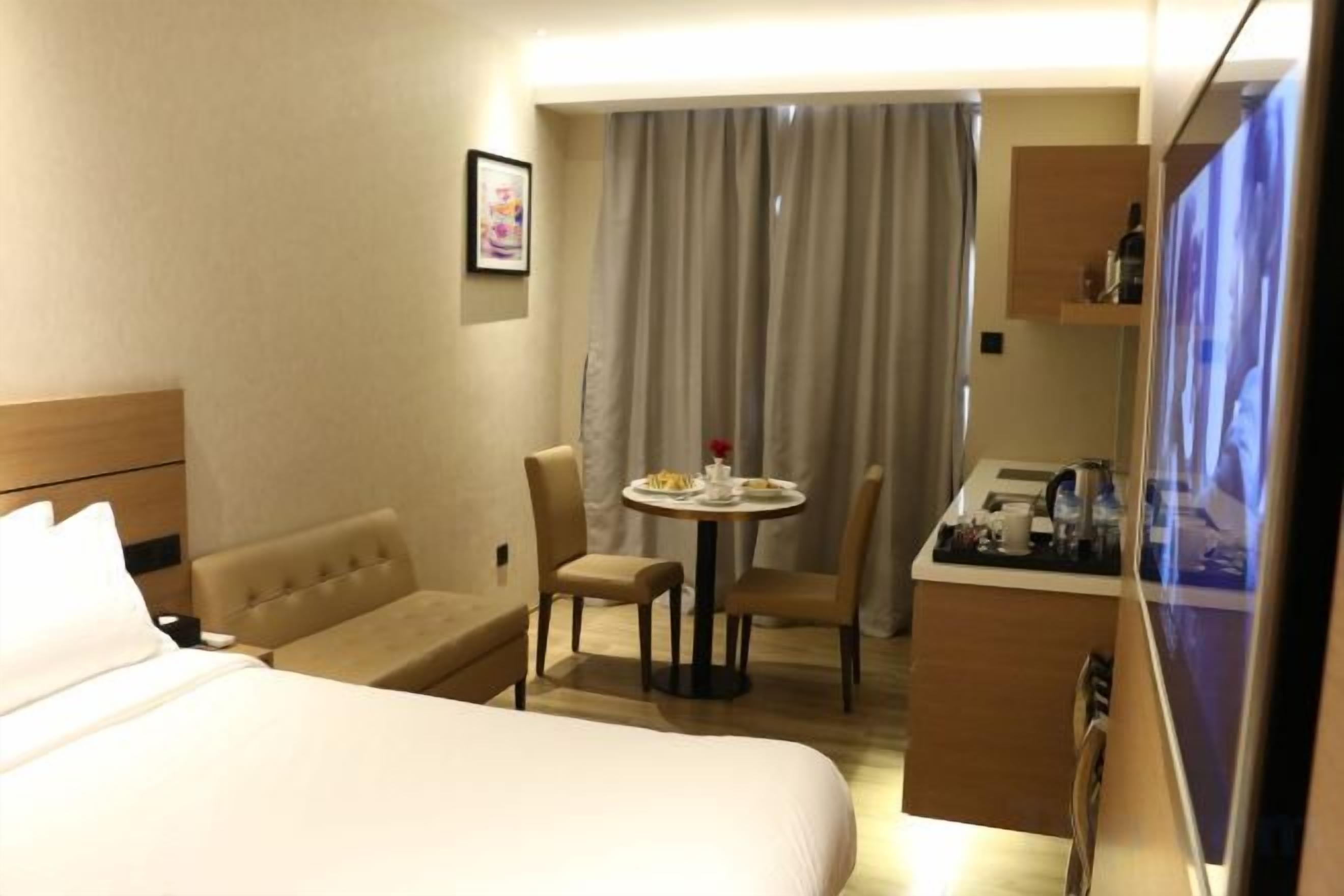 Quarto de hotel com cama, área de estar com mesa, televisão e cozinha compacta.