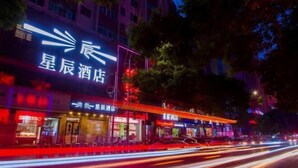 Hotel com placa visível, área de estar externa e rua movimentada com rastros de luz.