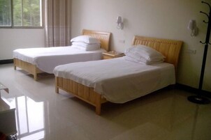Quarto de hotel com duas camas de solteiro, uma mesinha de cabeceira e um abajur.