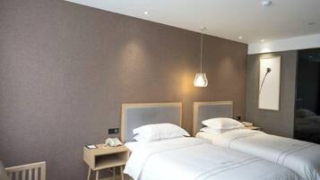 Quarto de hotel com duas camas, uma escrivaninha com telefone e um lustre.