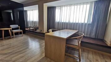 Quarto de hotel moderno com mesa de jantar de madeira, duas cadeiras, uma mesinha lateral e um espelho grande.