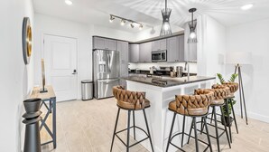 Uma cozinha moderna com eletrodomésticos de aço inoxidável, uma ilha central com banquetas e iluminação embutida no teto.