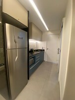 Uma cozinha compacta com geladeira de aço inoxidável, forno embutido e pia.