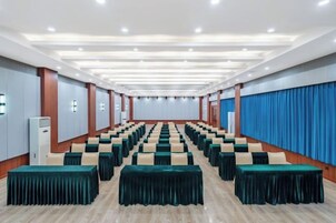 Sala de conferência com mesas e cadeiras dispostas em fileiras, um púlpito e um fundo de cortina azul.