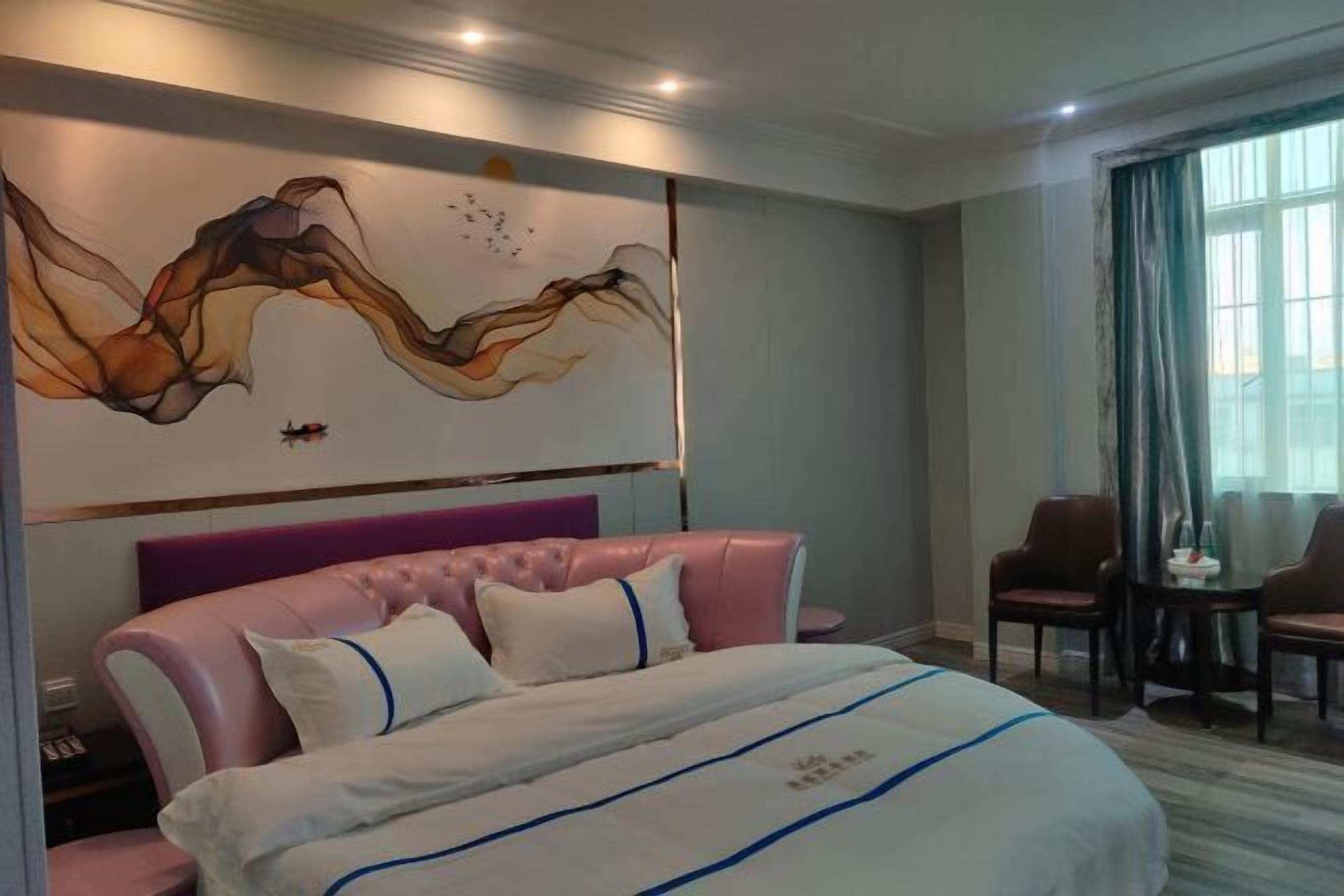Quarto de hotel com uma cama grande, cabeceira, área de refeições com cadeiras e uma parede com um quadro.