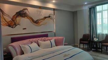 Quarto de hotel com uma cama grande, cabeceira, área de refeições com cadeiras e uma parede com um quadro.