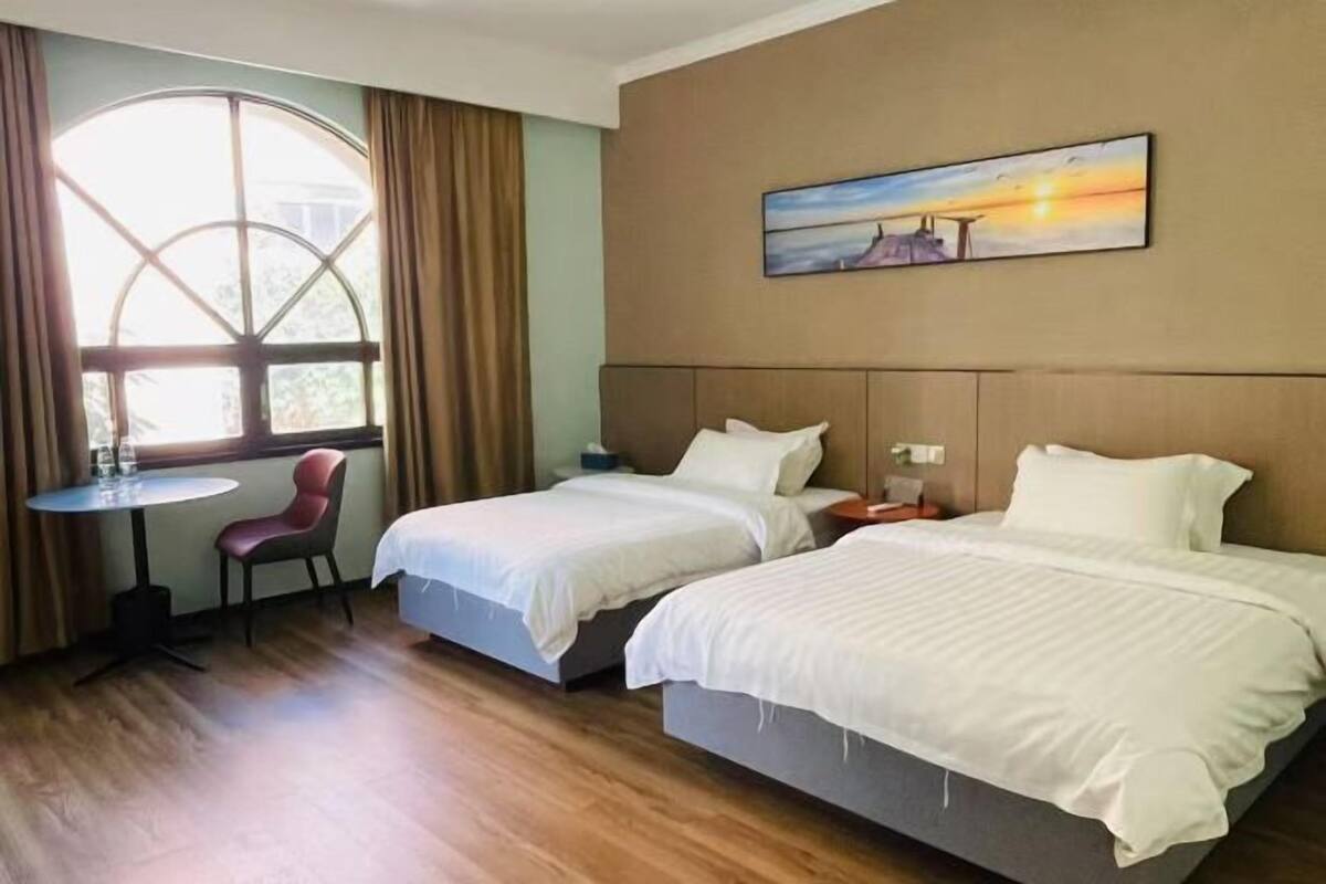 Quarto de hotel com duas camas, uma mesa redonda, uma cadeira e uma janela com cortinas.