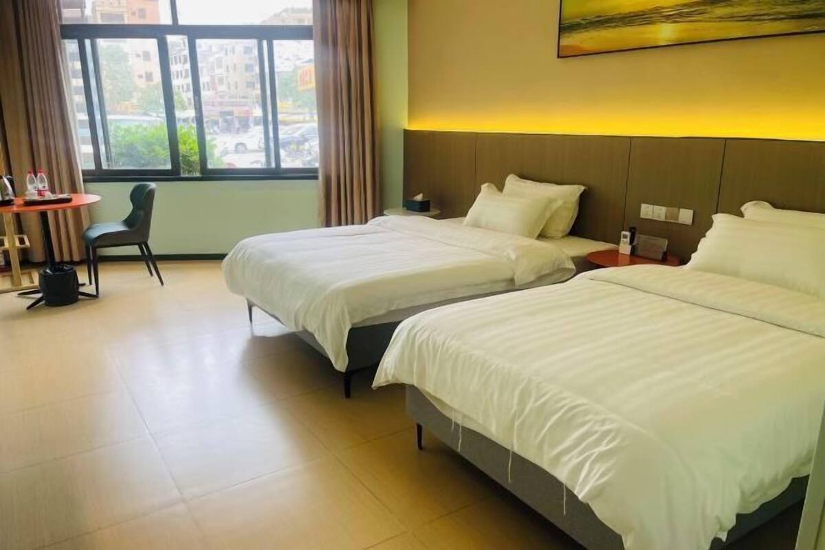 Quarto de hotel com duas camas, uma escrivaninha, uma cadeira e uma janela com vista para a cidade.