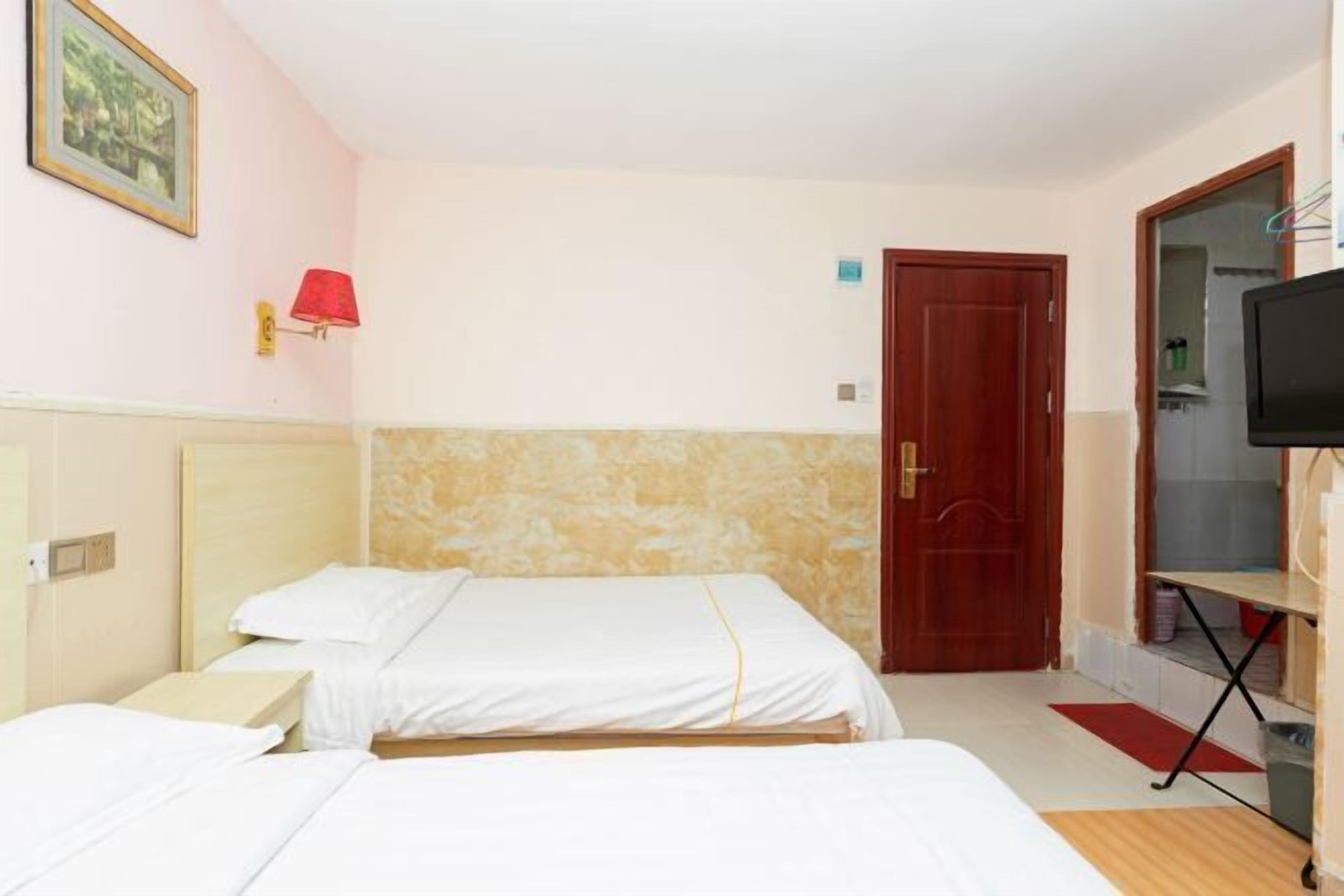 Quarto de hotel com duas camas, uma televisão, um abajur vermelho e uma porta de madeira.