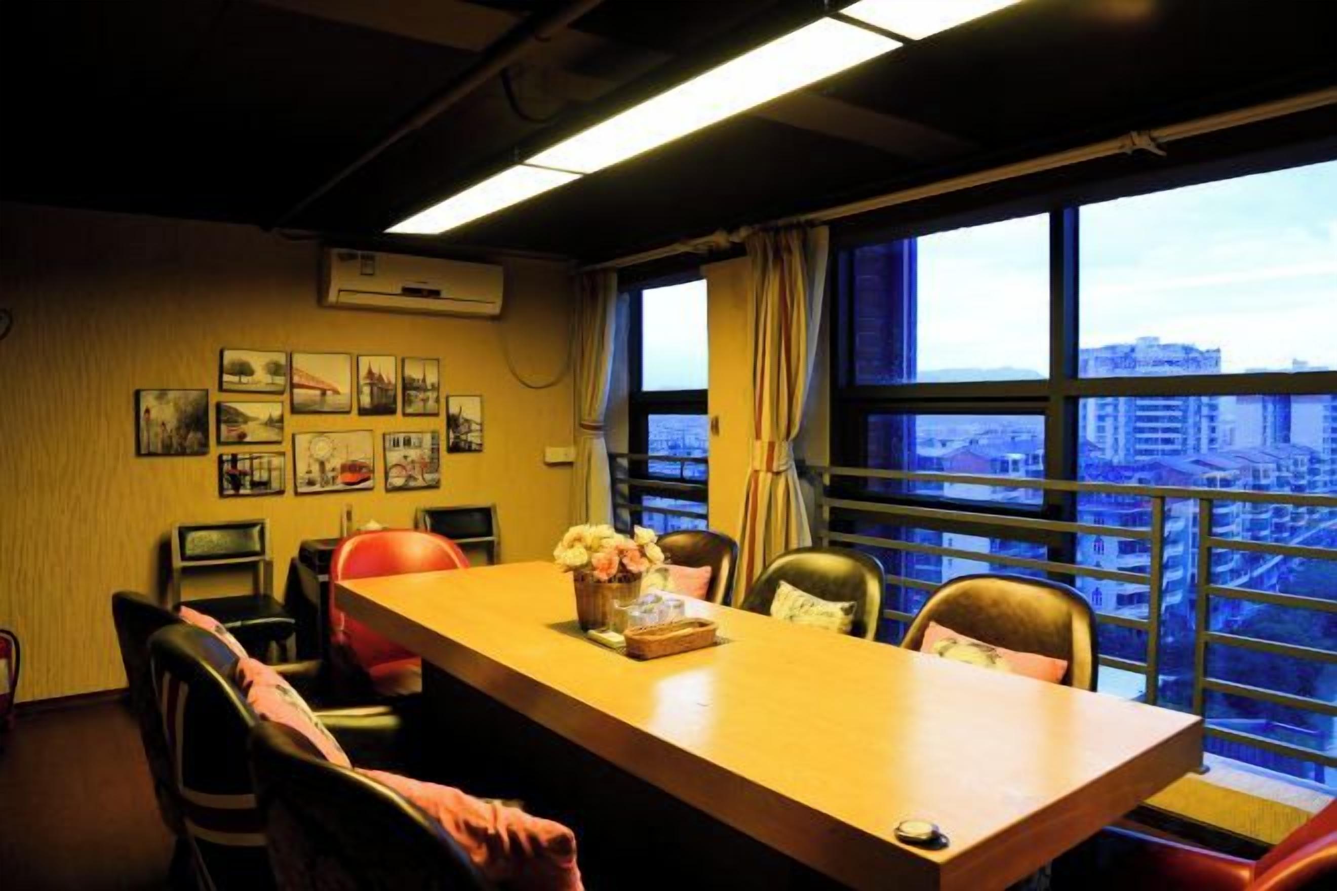Sala de conferências com uma mesa comprida, cadeiras e vista para a cidade através de grandes janelas.