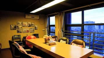 Sala de conferências com uma mesa comprida, cadeiras e vista para a cidade através de grandes janelas.