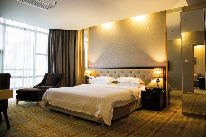 Quarto de hotel com uma cama grande, uma cadeira, uma escrivaninha e um espelho.