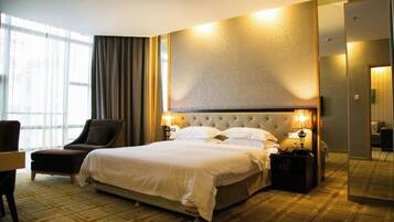 Quarto de hotel com uma cama grande, uma cadeira, uma escrivaninha e um espelho.