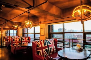 Restaurante com assentos em cabines, bandeiras britânicas, amplas janelas e luminárias pendentes esféricas.