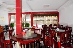 Um espaço de refeições de hotel com mesas e cadeiras redondas, um pilar grande e uma janela com cortinas.