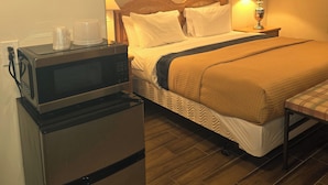 Quarto de hotel com cama, mesa de cabeceira com luminária, micro-ondas e geladeira.
