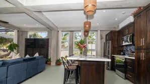 Cozinha moderna com armários de madeira escura, uma ilha central e um sofá azul na sala de estar.