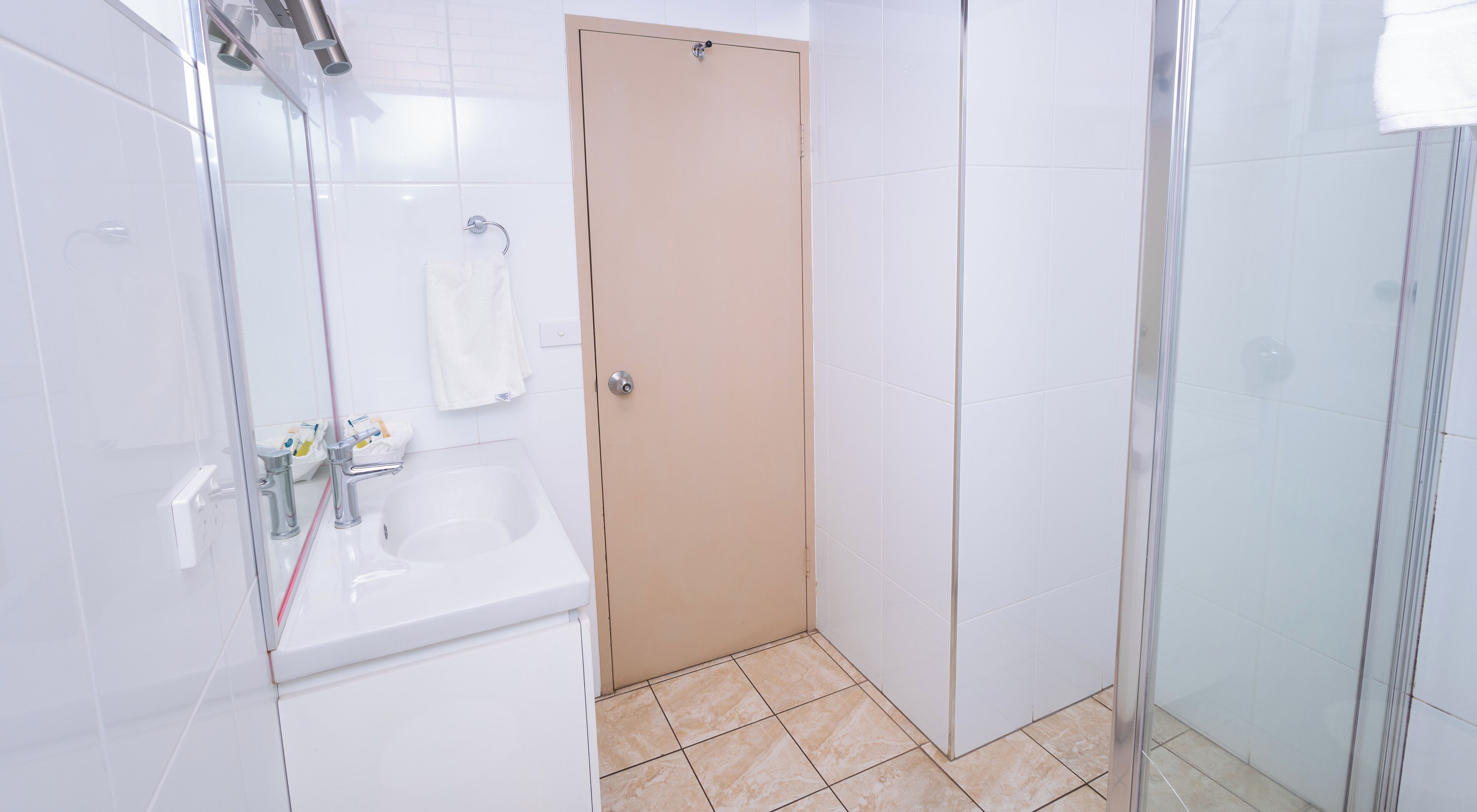 Casa de banho com lavatório branco, cabine de duche em vidro e porta bege.