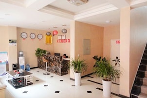 Uma área de recepção com balcão, bebedouro, relógio e placa com o nome do hotel.