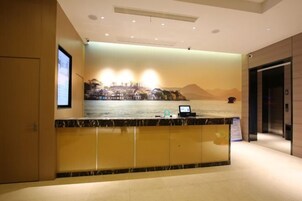 Balcão de recepção com um grande mural de uma paisagem costeira, uma tela digital e uma pequena mesa com um computador.