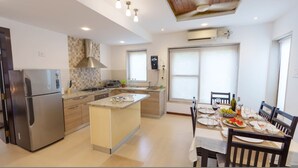 Uma cozinha moderna com ilha central, eletrodomésticos de aço inoxidável e uma área de jantar com mesa posta para quatro pessoas.