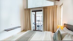 Quarto de hotel com uma cama, uma mesinha e vista para a varanda.