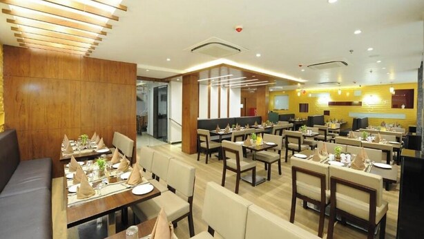 Um restaurante com várias áreas de refeição, painéis de madeira e luminárias modernas.