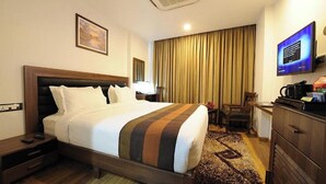 Quarto de hotel com cama, escrivaninha, televisão e máquina de café.
