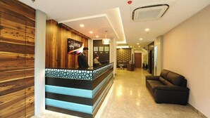 Área de recepção de hotel com parede de painéis de madeira, balcão de recepção, sofá e corredor que dá acesso a outros quartos.