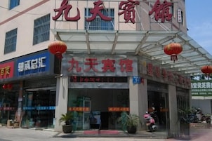 Hotel com grande placa, entrada coberta e plantas em vasos na frente.