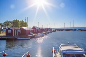 Uma marina com vários edifícios pequenos vermelhos, barcos atracados e um céu claro.