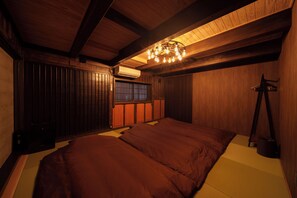 Um quarto em estilo japonês tradicional, com piso de tatame, cama com cobertor marrom, teto de madeira e luminária pendente.