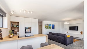 Um espaço de estar moderno com cozinha, mesa de jantar, sofá e televisão de tela plana na parede.