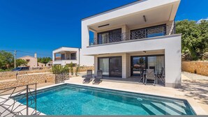 Uma casa moderna de dois andares com piscina, área de estar externa e um muro de pedra.