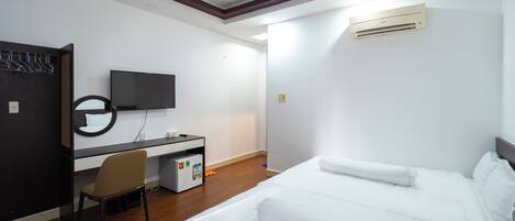Quarto de hotel com cama, escrivaninha, cadeira, televisão e ar condicionado.