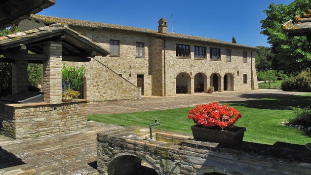 Um edifício de pedra com telhado em telhas, janelas em arco e um pátio pavimentado com uma ponte de pedra.