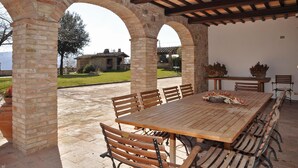 Pátio externo com mesa e bancos de madeira, rodeado por arcos de tijolo e uma pérgula.