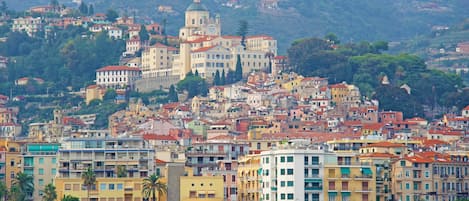 Paisagem costeira com uma igreja imponente numa colina, edifícios coloridos e uma área de praia com guarda-sóis.