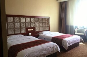 Quarto de hotel com duas camas, cabeceira com desenho estampado, uma cadeira e vista para o exterior.