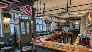 Uma área de bar com balcão de madeira, banquetas e uma exposição de copos.