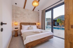 Quarto com parede de pedra, estrutura de cama de madeira, duas luminárias de cabeceira, mesa de cabeceira e vista para uma piscina ao ar livre.