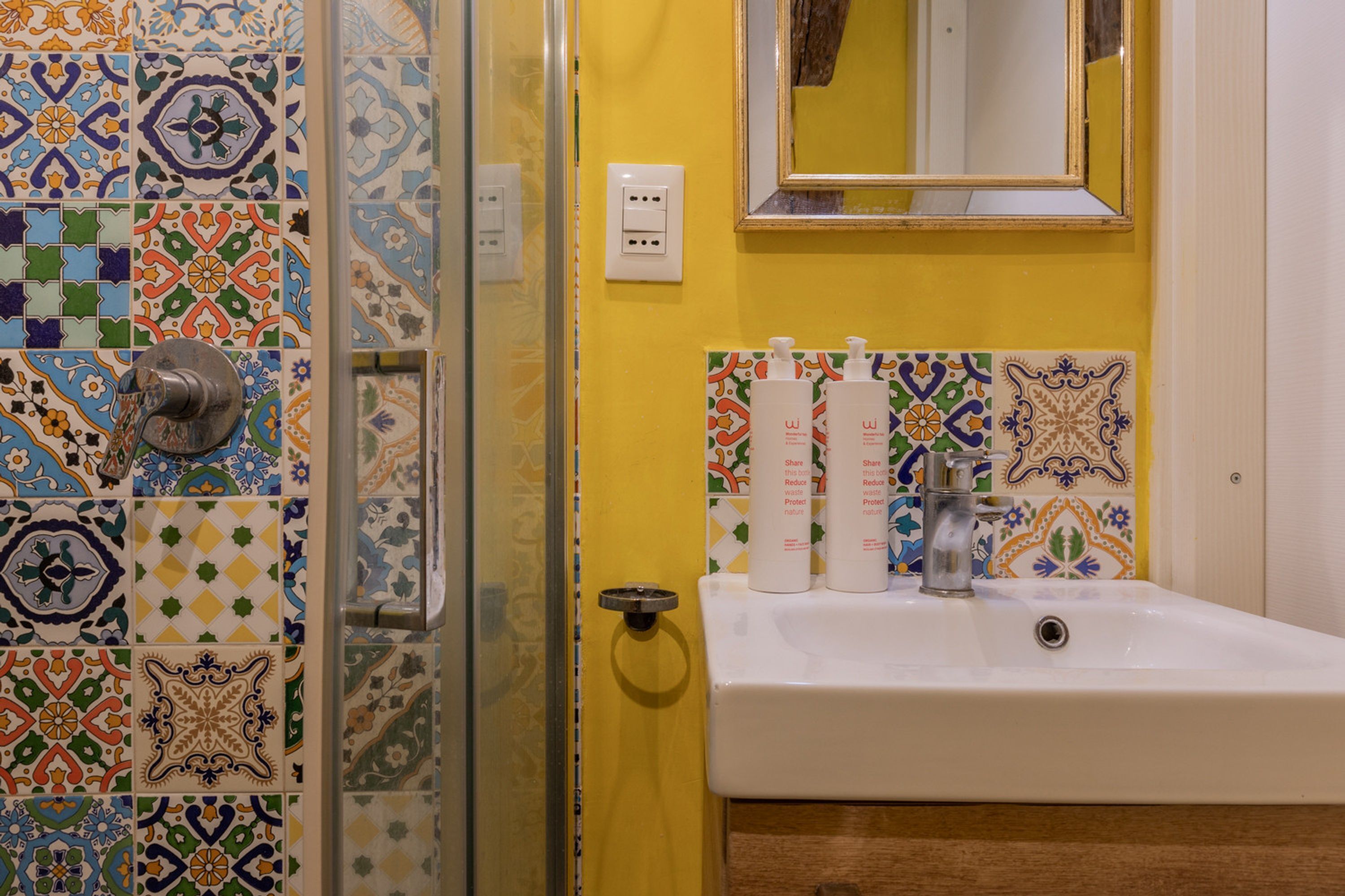 Casa de banho com parede revestida em azulejo, pia e espelho.