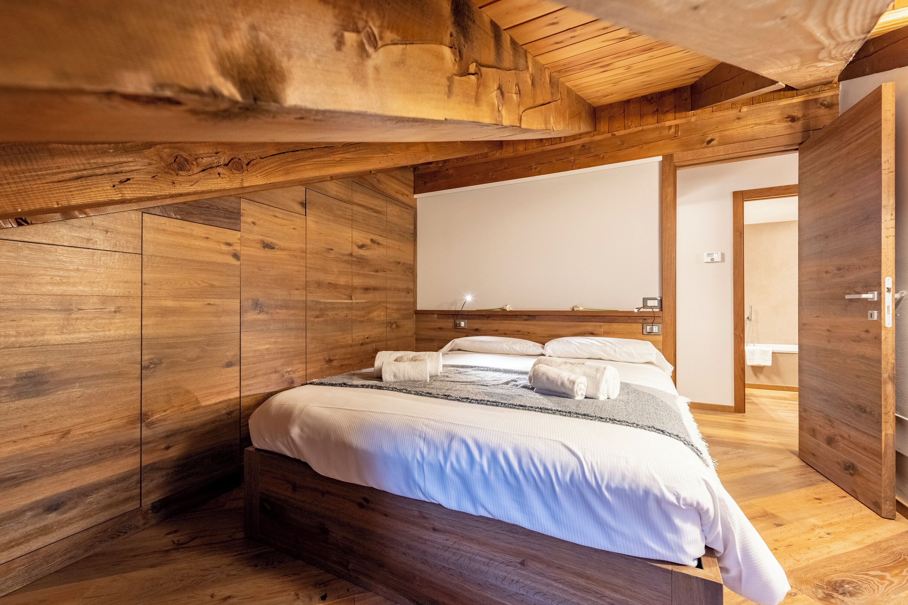 Quarto de madeira com cama, paredes de madeira e um espelho grande.
