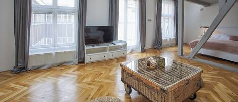 Quarto espaçoso com uma grande janela, televisão, piso de madeira, mesa de centro de vime e uma cama beliche.