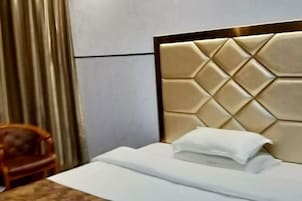 Cama bem arrumada com cabeceira acolchoada, uma cadeira de madeira e uma cortina ao fundo.